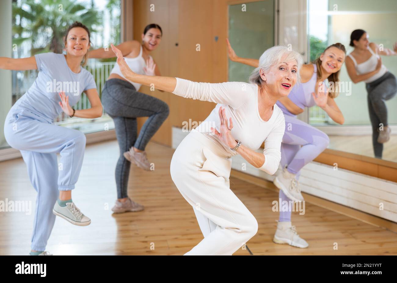 Mature female coach dancing and practicing new movements with group of ...