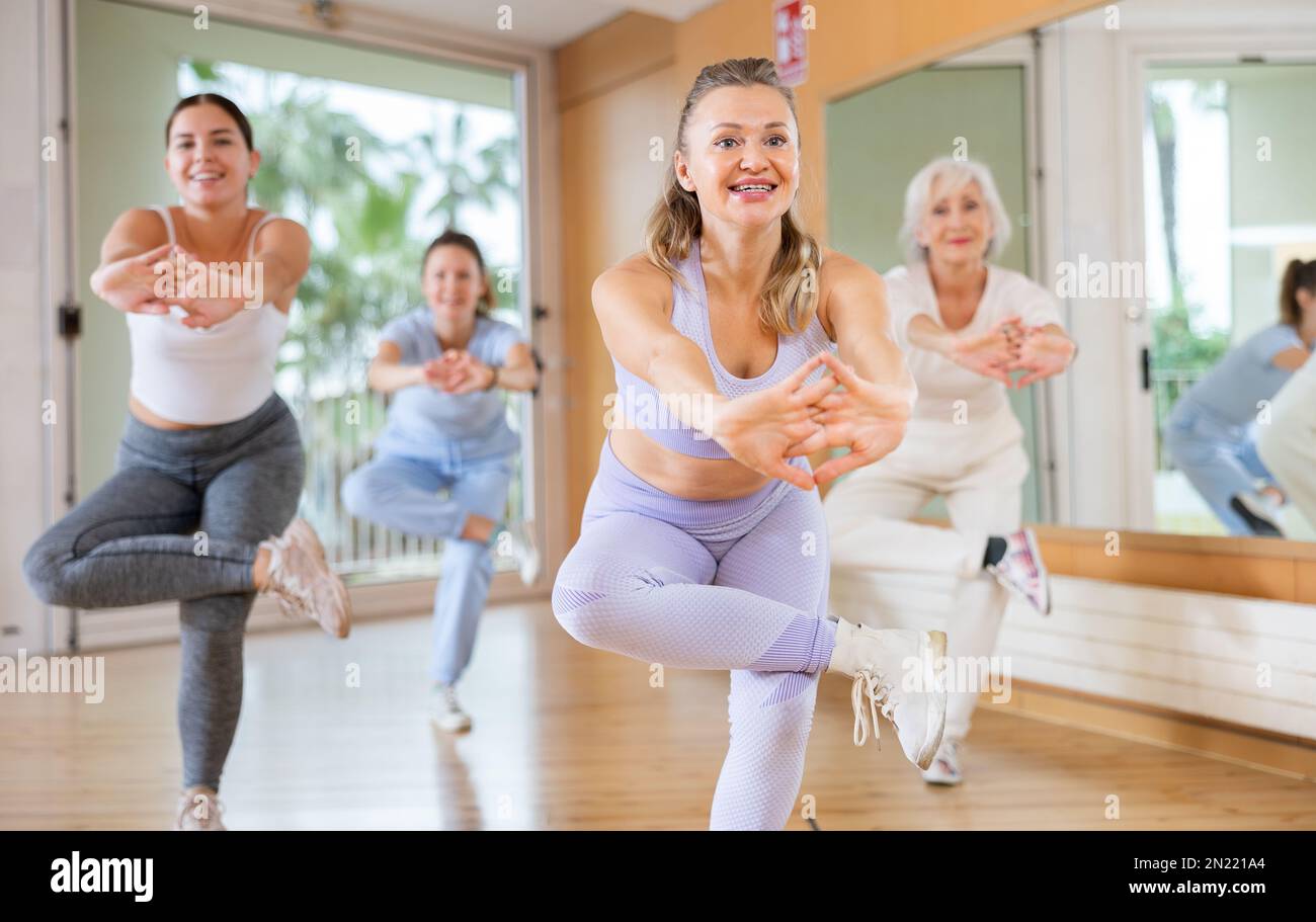 Group of smiling women of different ages dancing and practicing new movements in class. Sport ...