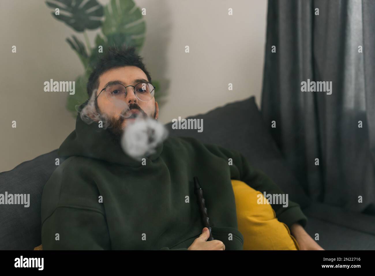Bearded millennial or gen z man smoking hookah while relaxing on sofa ...