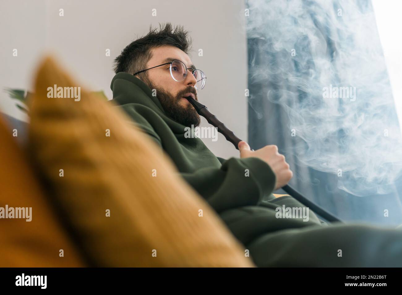 Bearded millennial or gen z man smoking hookah while relaxing on sofa ...