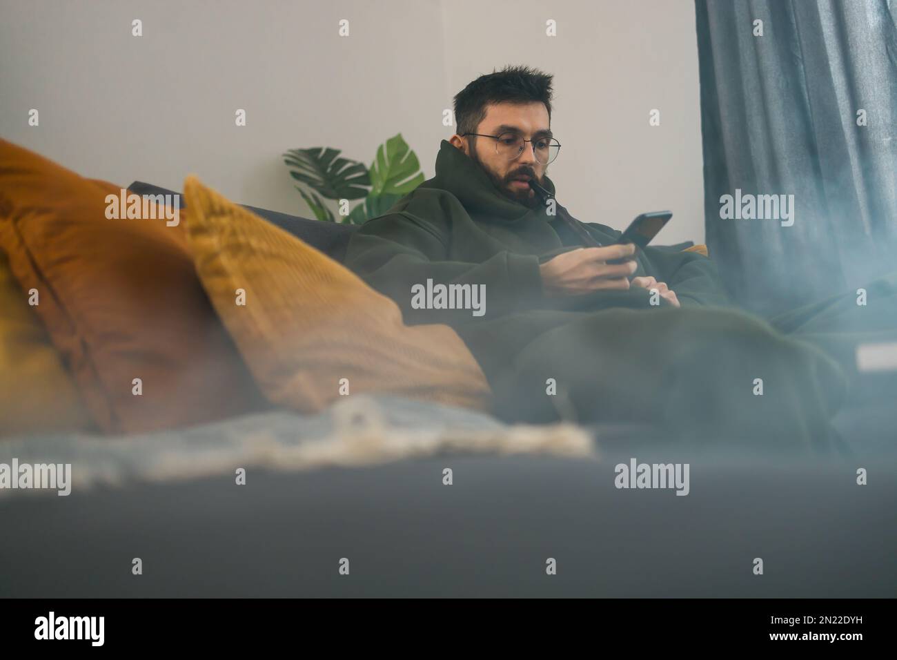 Bearded millennial or gen z man smoking hookah while relaxing on sofa ...