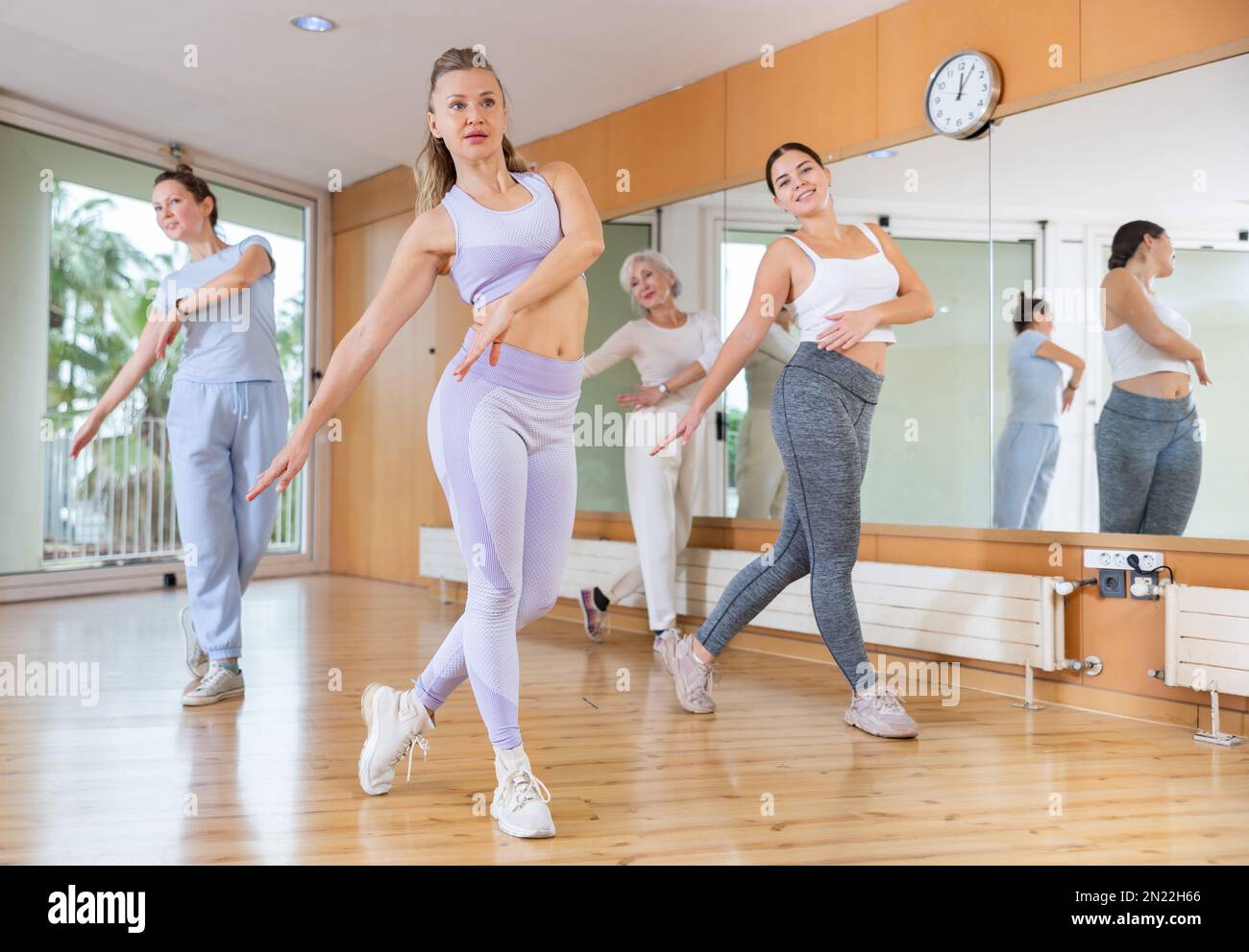 Energetic female dancers of different ages learning new dancing steps in modern fitness class ...