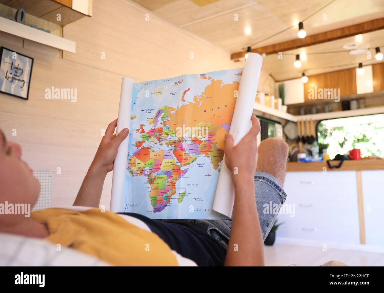 Young traveler with world map planning trip on bed in motorhome ...