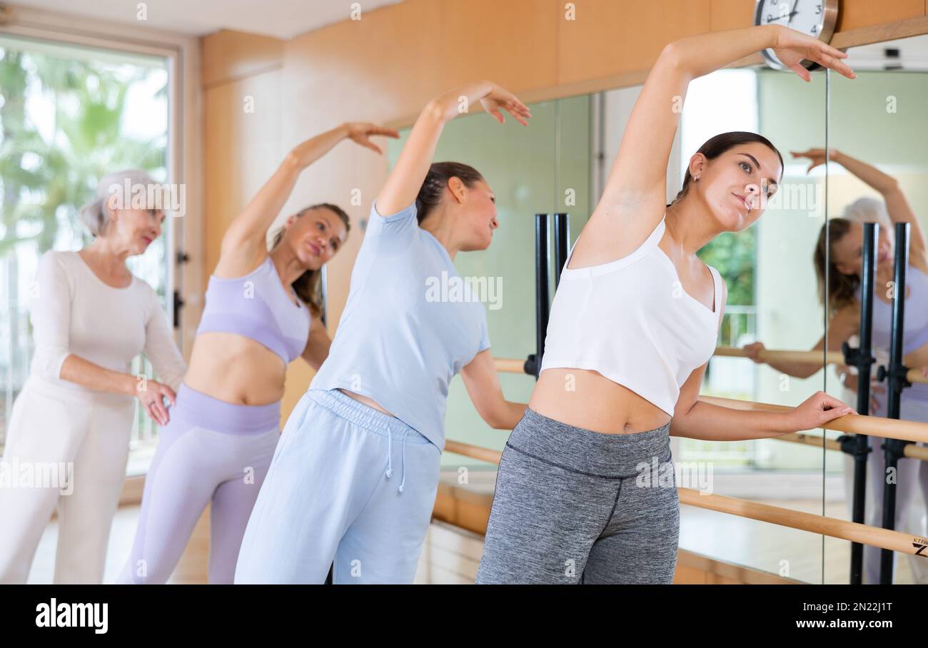 Focused sporty young women standing near ballet barre training ...