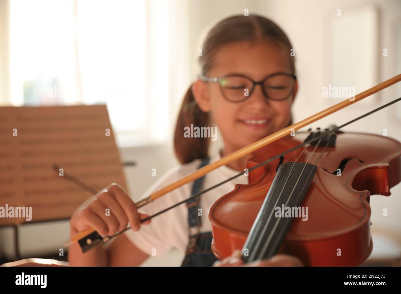 Cute little girl playing violin indoors. Music lesson, focus on strings ...