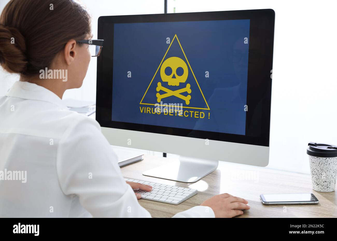 Office worker in front of computer with warning about virus attack on ...