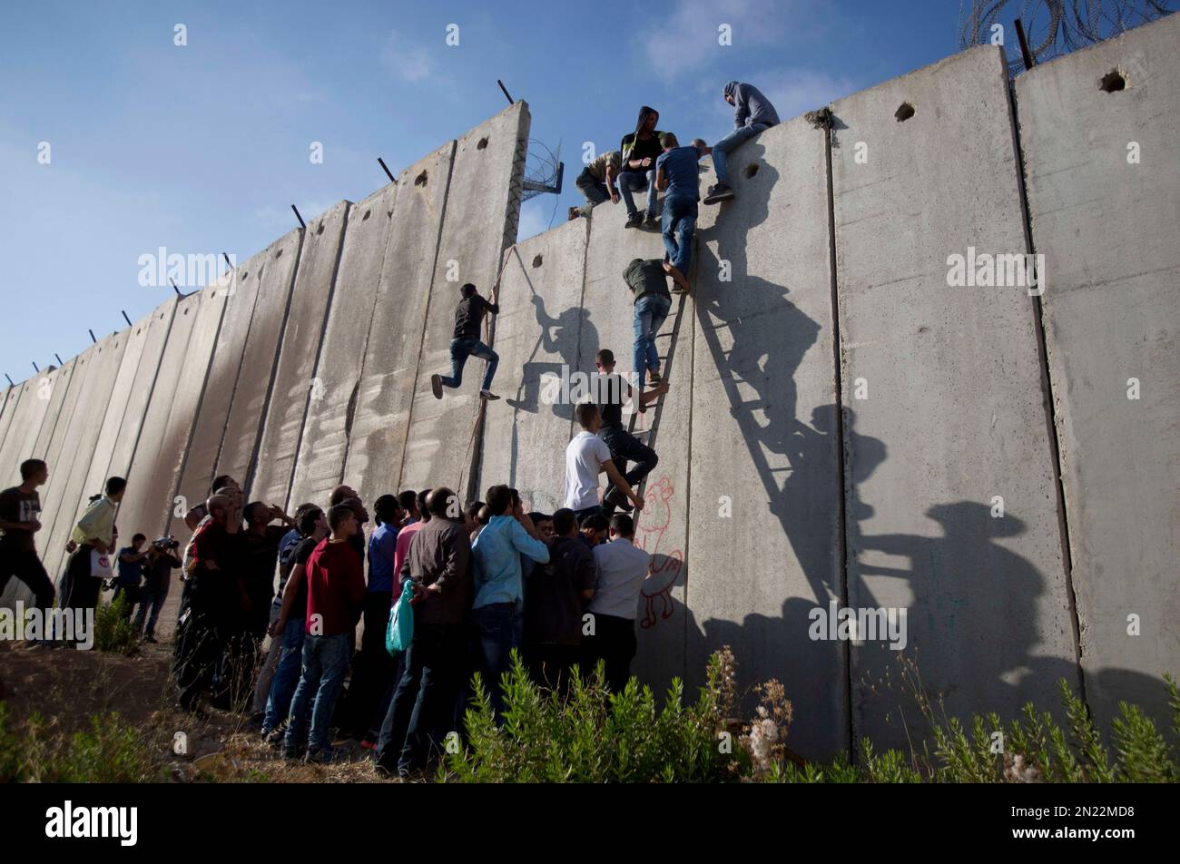 Palestinians use a ladder to climb over the separation barrier with ...
