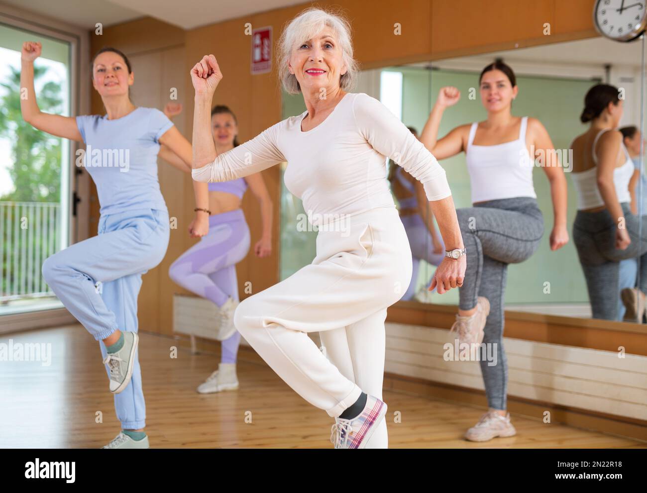 Mature female coach dancing and practicing new movements with group of ...