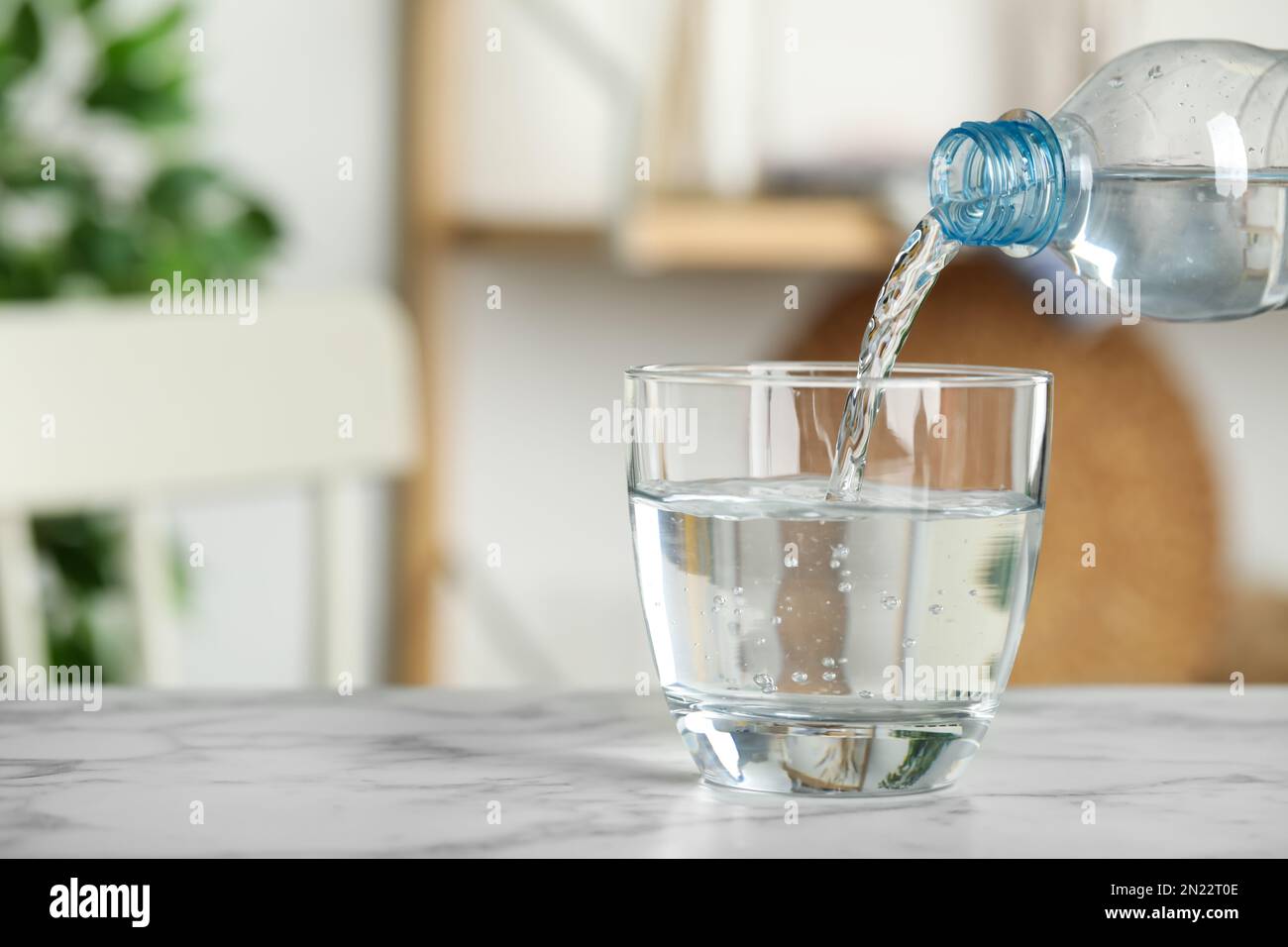 Pouring water from bottle into glass on white marble table indoors, space for text. Refreshing ...