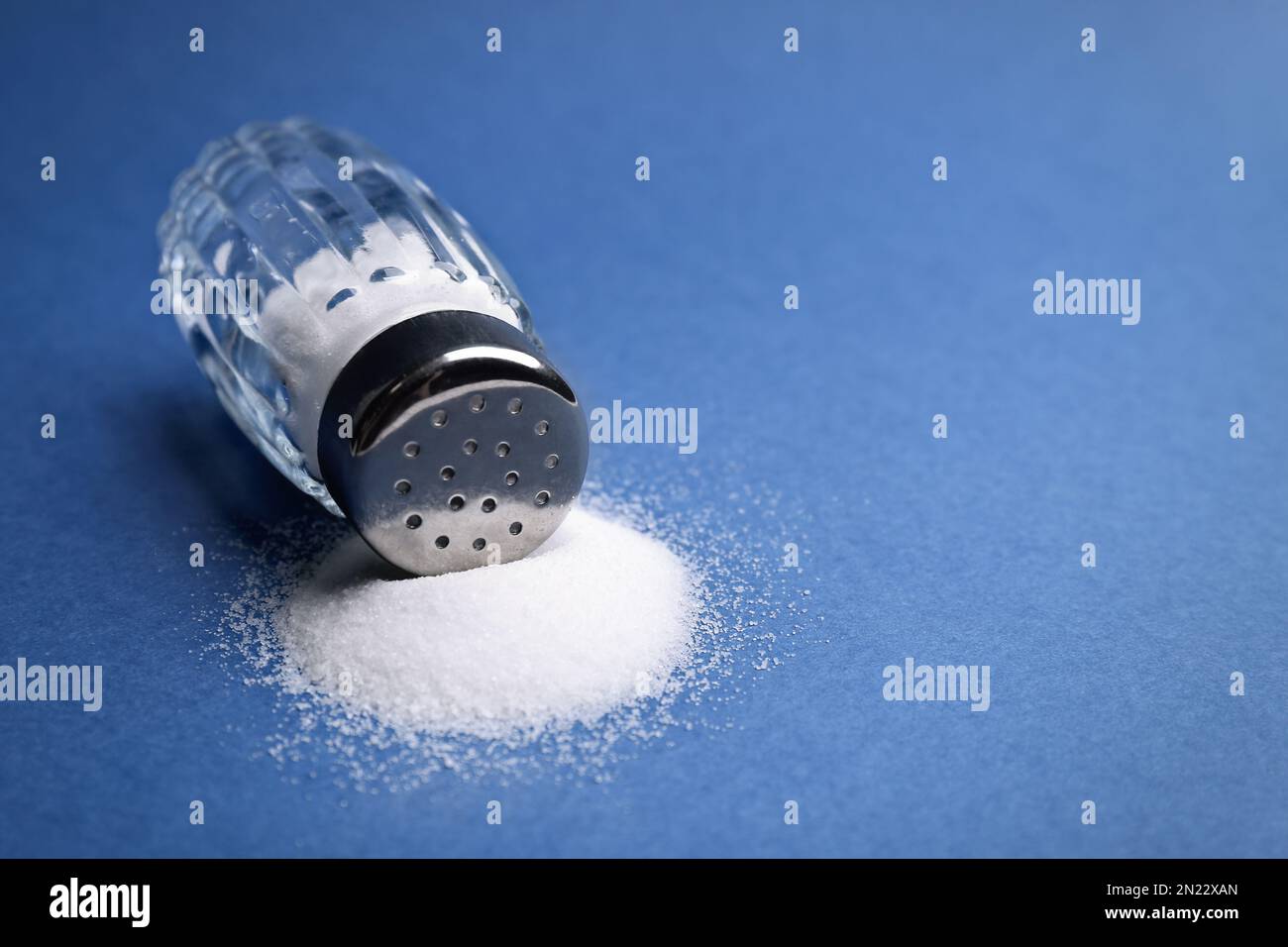 Scattered salt and shaker on blue background, closeup. Space for text ...