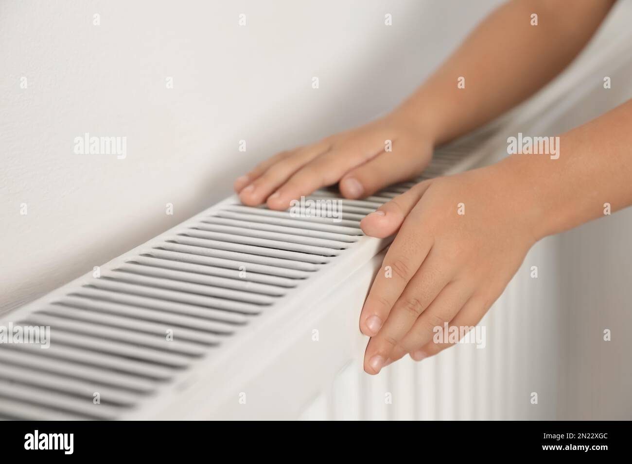 Child warming hands on heating radiator near white wall, closeup Stock ...