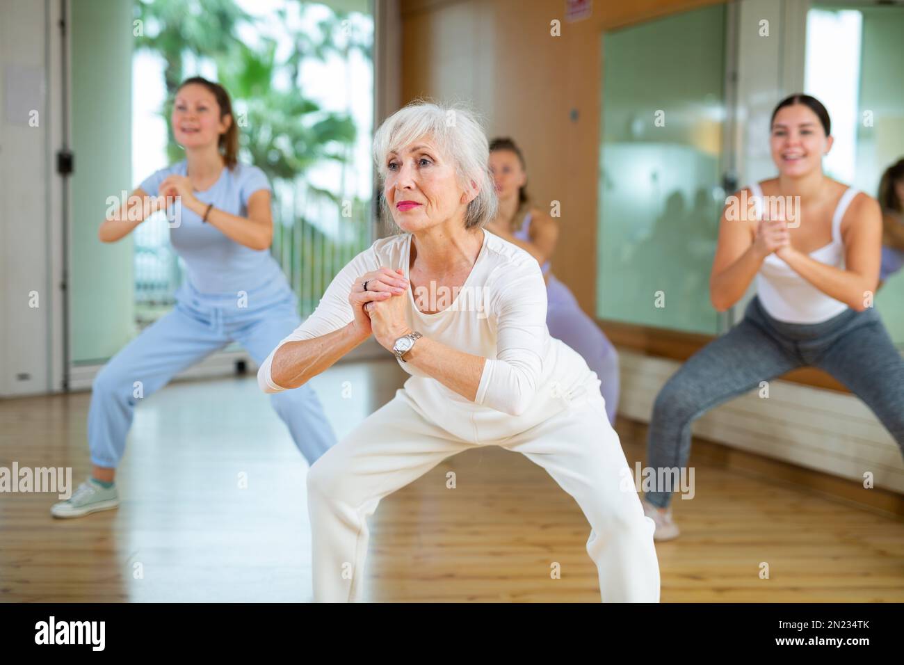 Mature female coach dancing and practicing new movements with group of ...