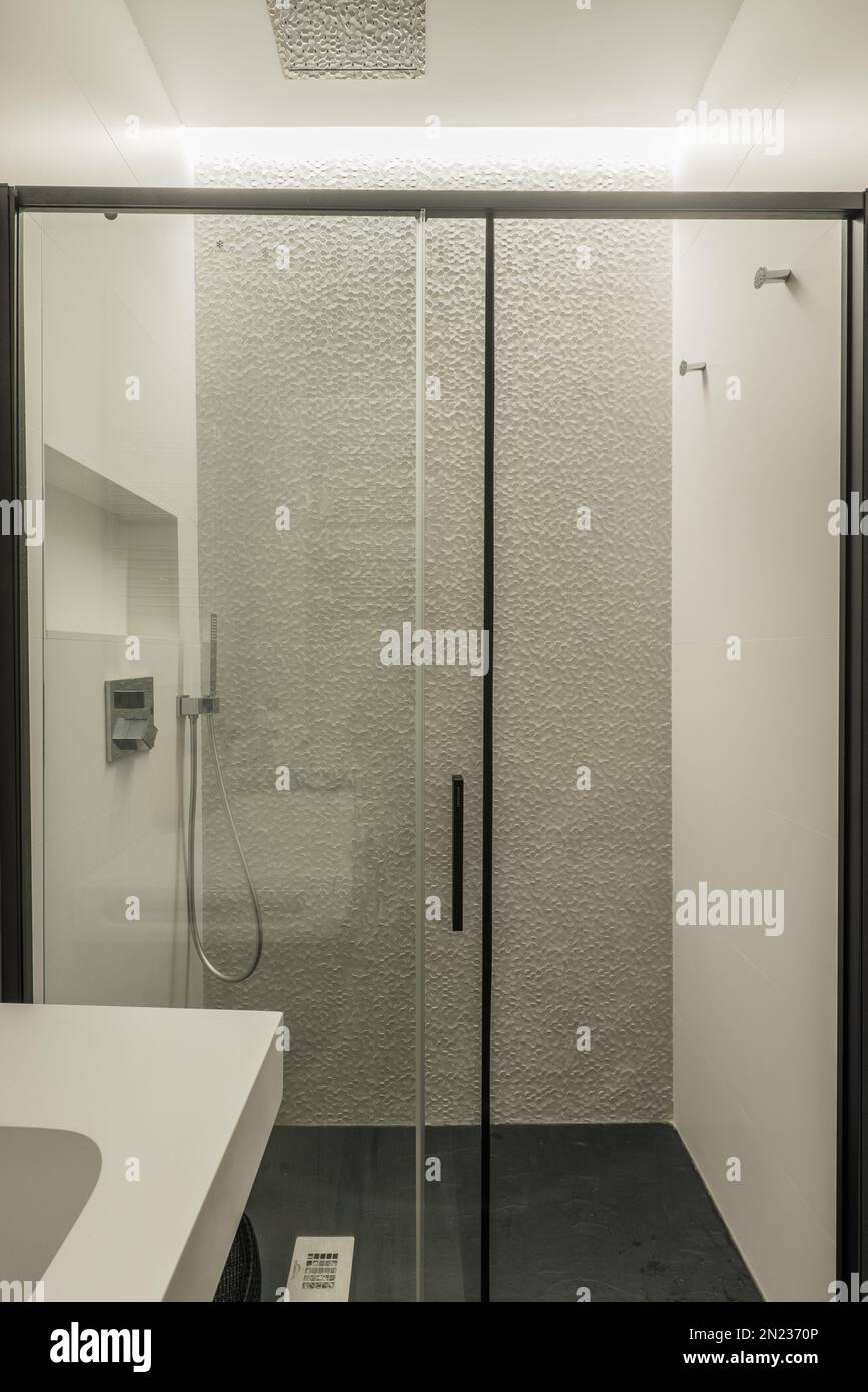 Shower cabin with rough white tiles, sliding glass partition with black ...