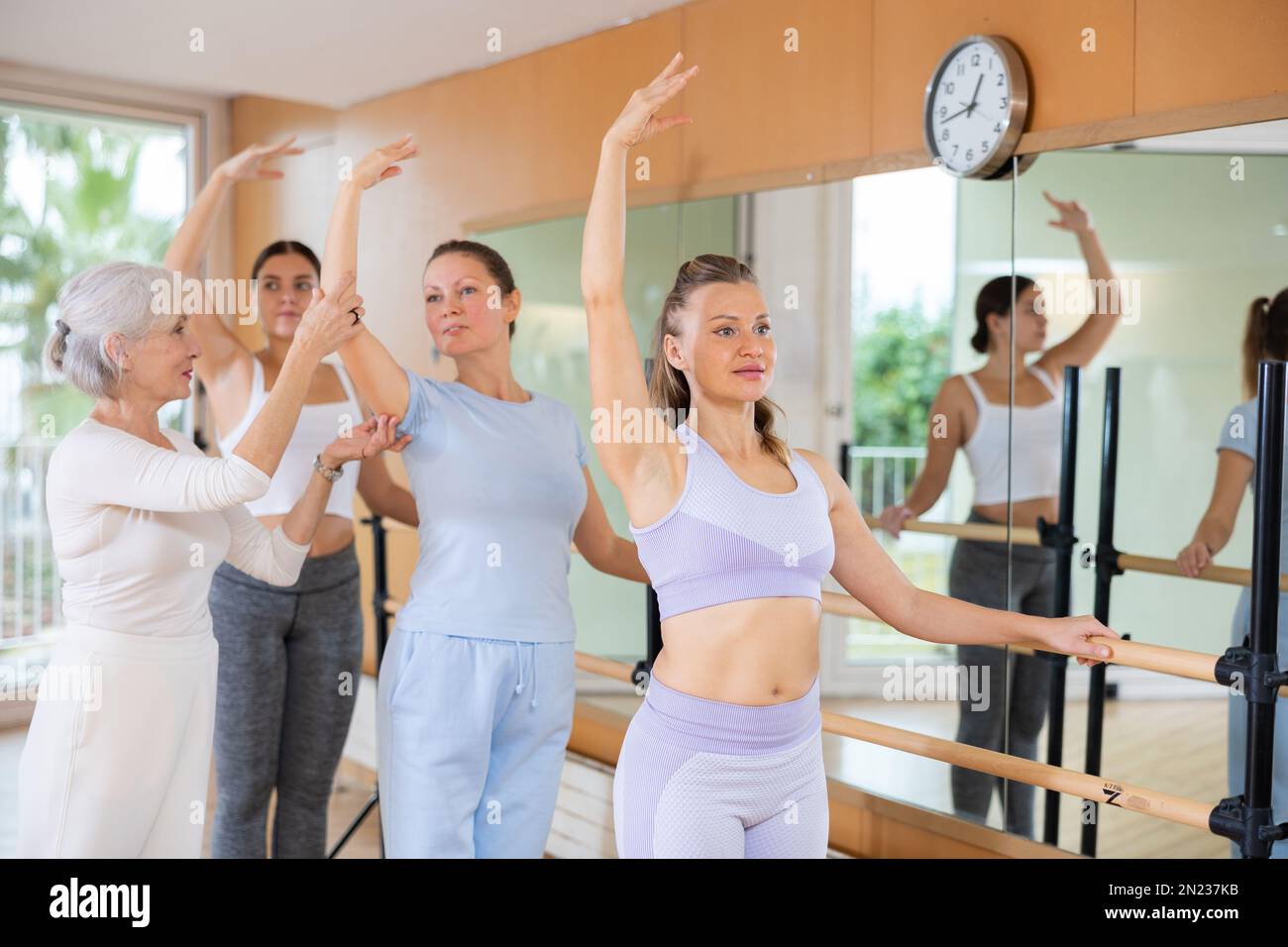 Focused sporty young women standing near ballet barre training ...