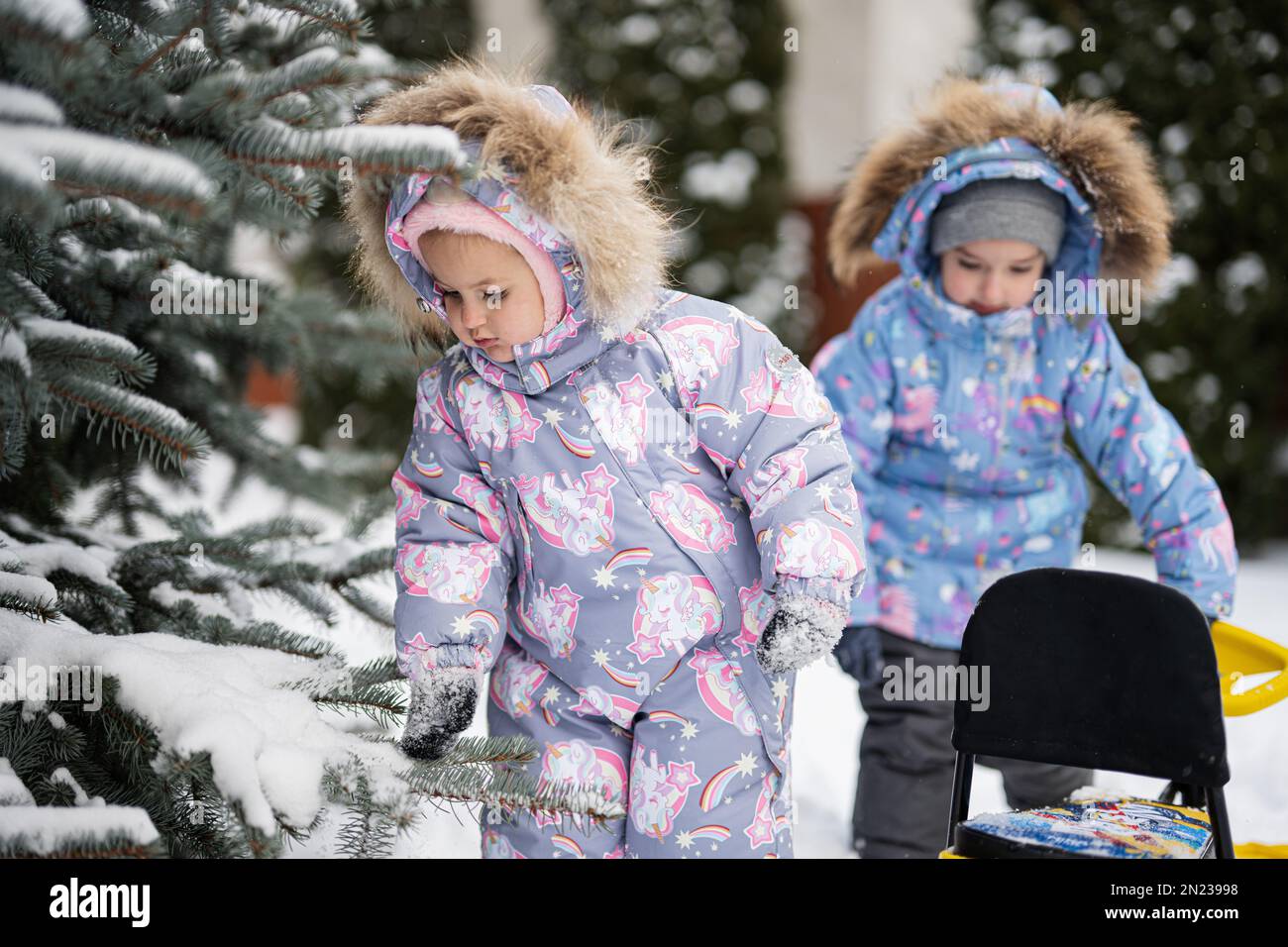Children play outdoors in snow. Two little sisters enjoy a sleigh ride ...