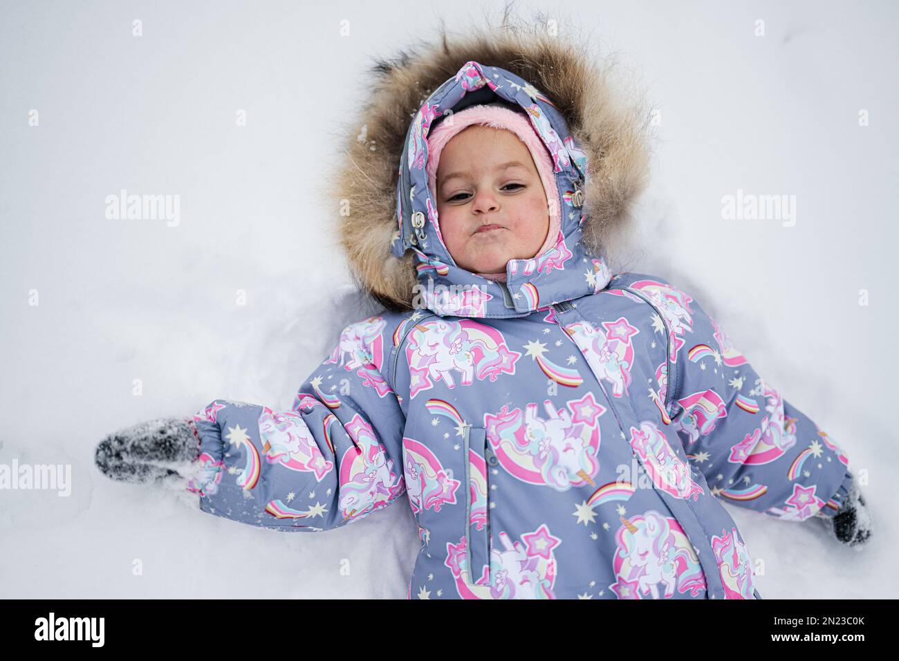 Baby girl making snow angel while lying on snow Stock Photo - Alamy
