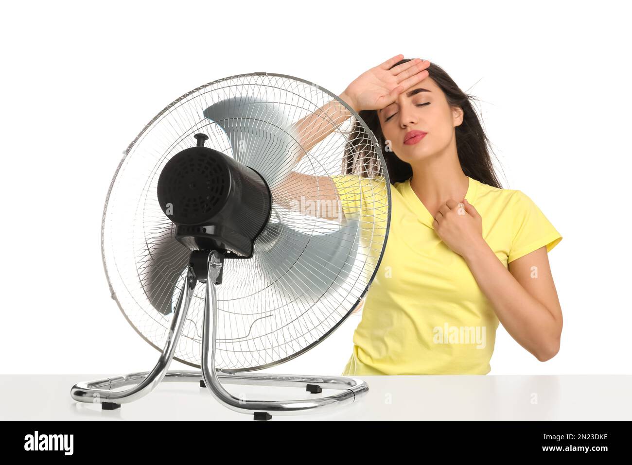 Woman suffering from heat in front of fan on white background. Summer ...