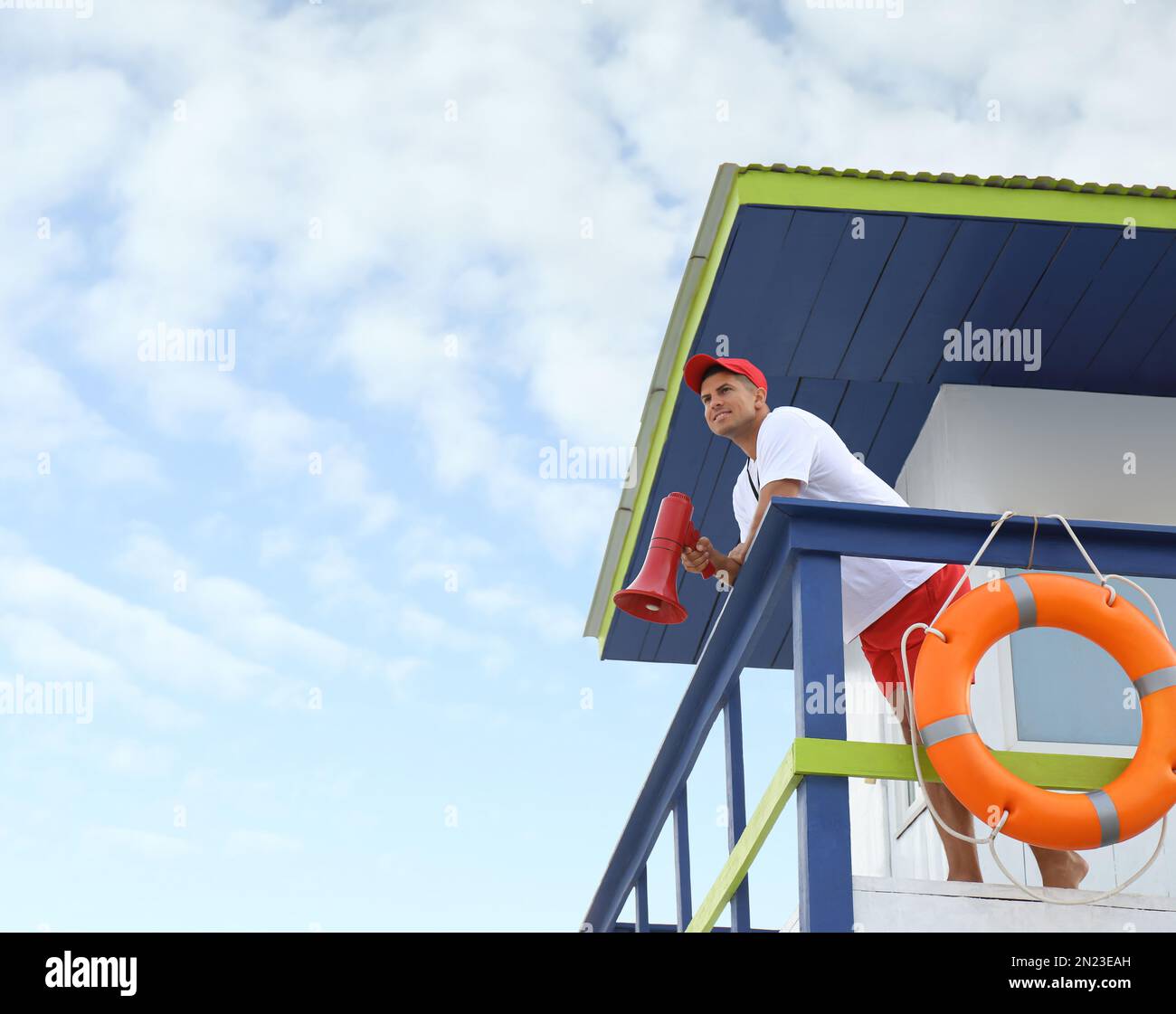 Male lifeguard with megaphone on watch tower against blue sky Stock ...
