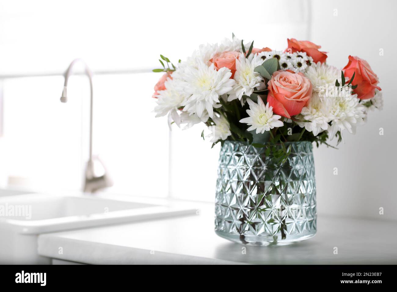 Vase with beautiful flowers on countertop in kitchen, space for text ...