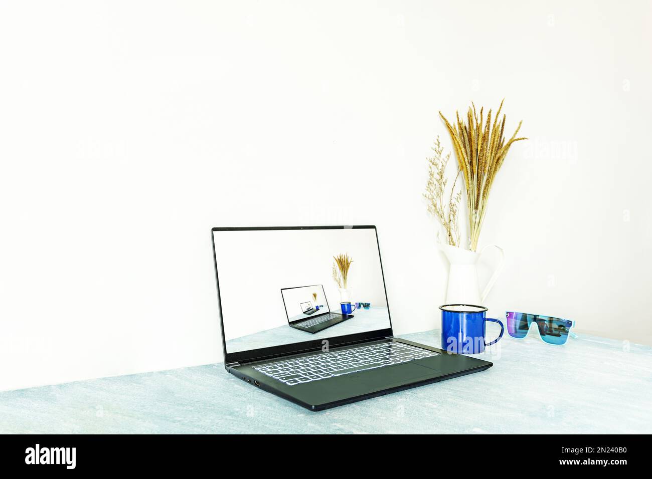 Image of a slim laptop next to a cup of coffee, a decorative metal mug ...