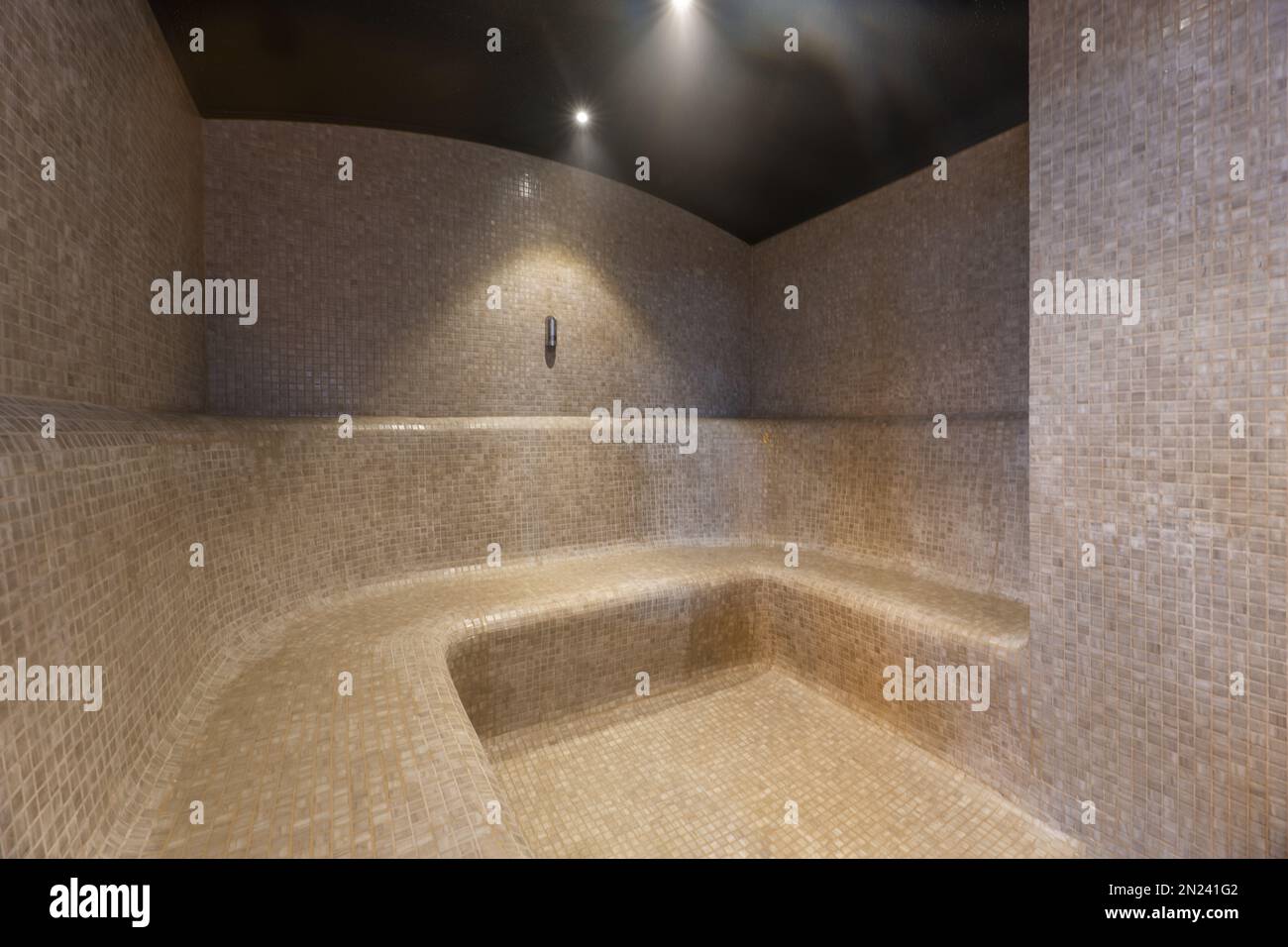 A cream and gray tiled sauna covering all surfaces and lamps on top ...