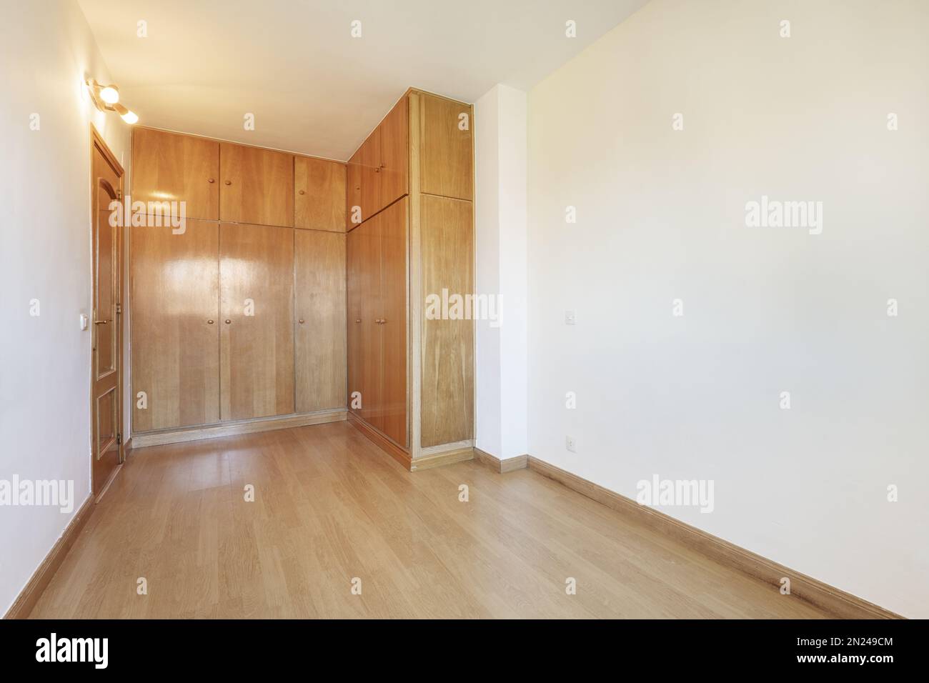 Empty white walled room with a custom made wardrobe covering two walls ...