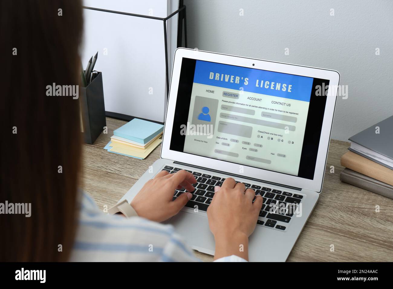 Woman using laptop to fill driver's license application form at table in office, closeup Stock ...