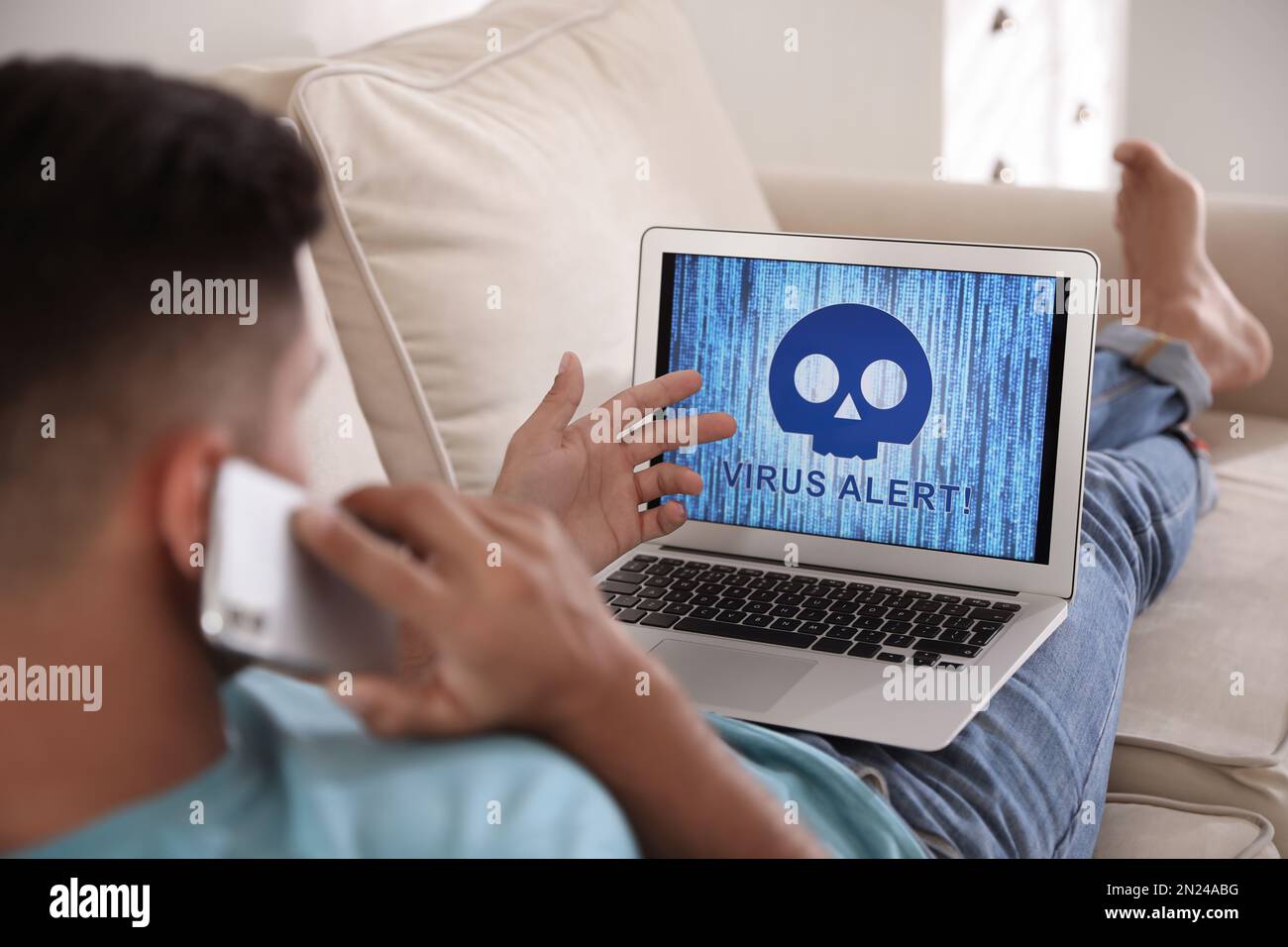 Man holding laptop with warning about virus attack on screen at home ...