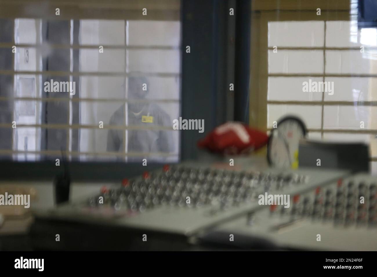A prisoner behind bars and thick plastic looks over at a corrections ...