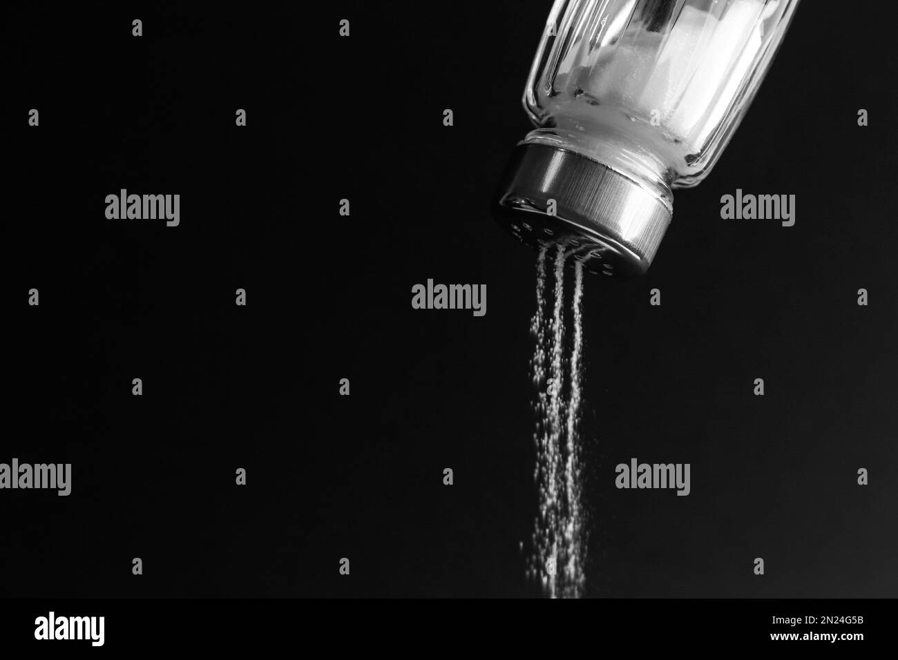 Pouring salt from shaker on black background, closeup. Space for text ...