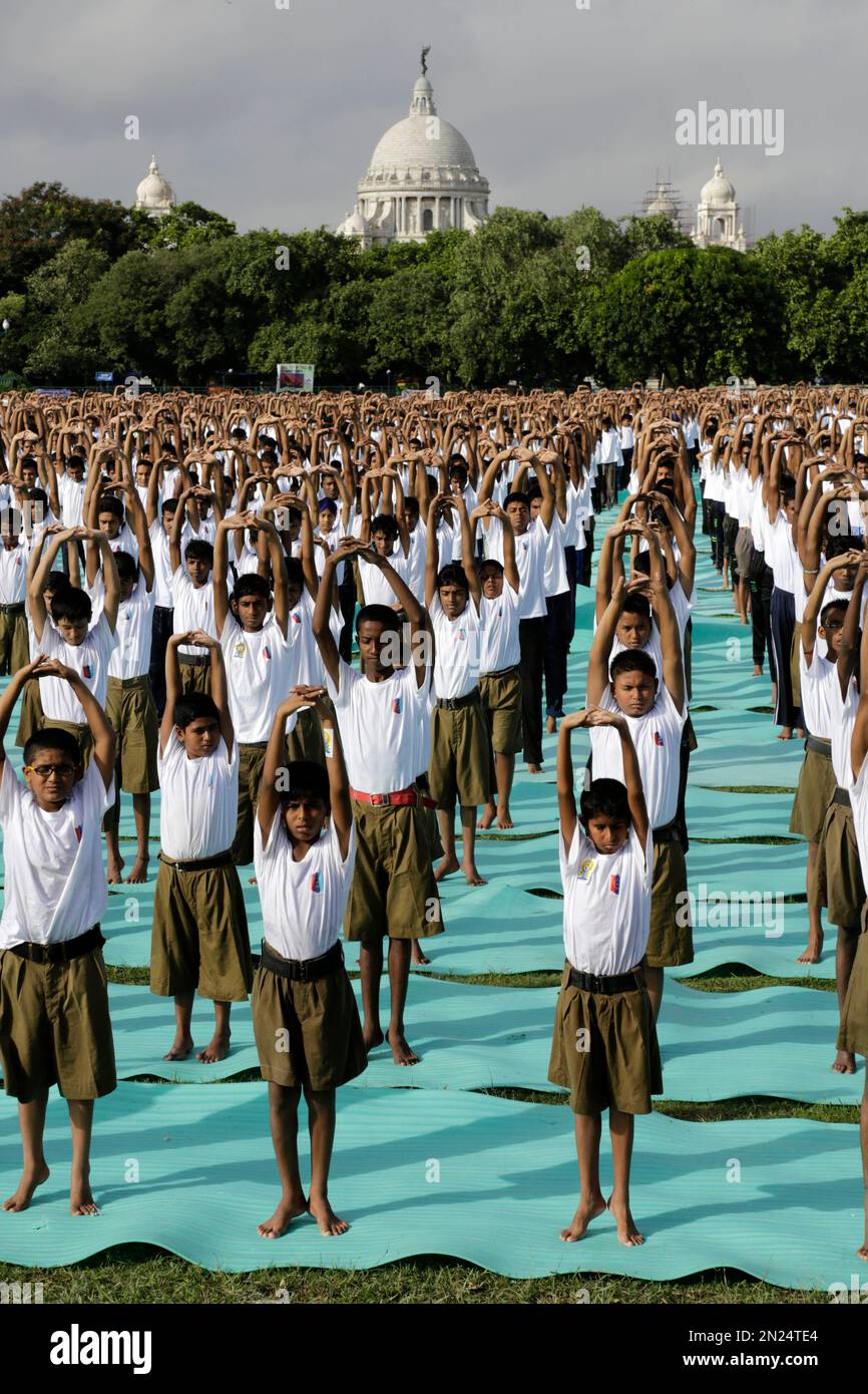Indian school children perform yoga in an open field beside city ...