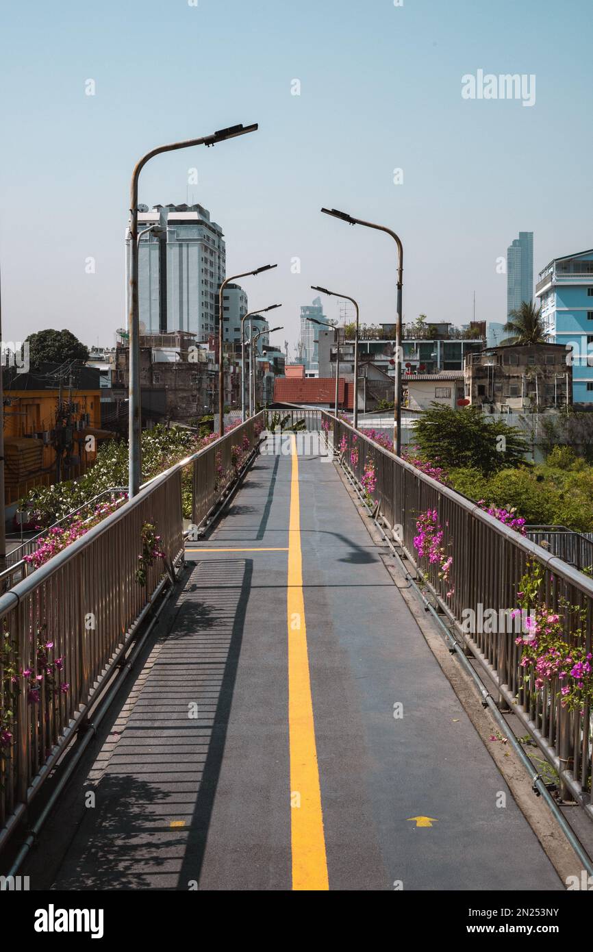 A bike path bridge in a city, surrounded by lots of plants and lamp ...