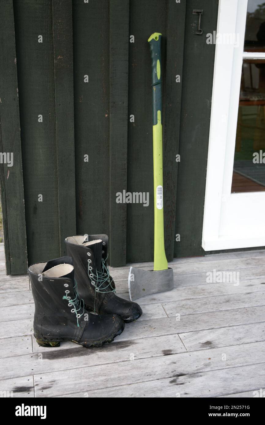 Old black boots and axe with bright green axe handle on deck of shed ...
