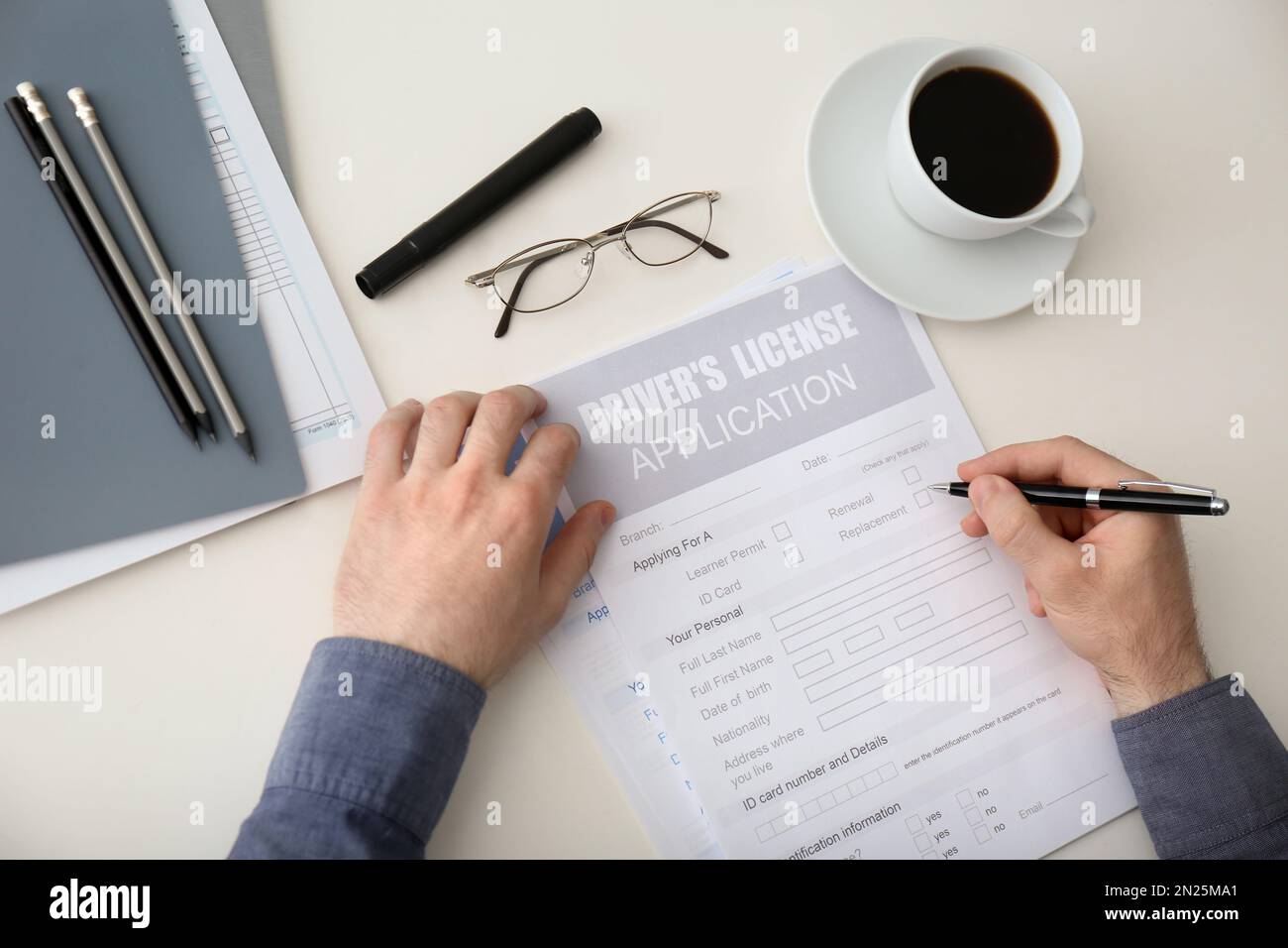 Man filling in driver's license application form at white table, above view Stock Photo - Alamy