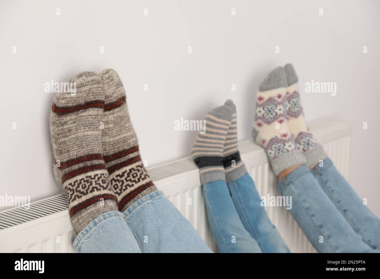 Family warming legs on heating radiator near white wall, closeup Stock ...