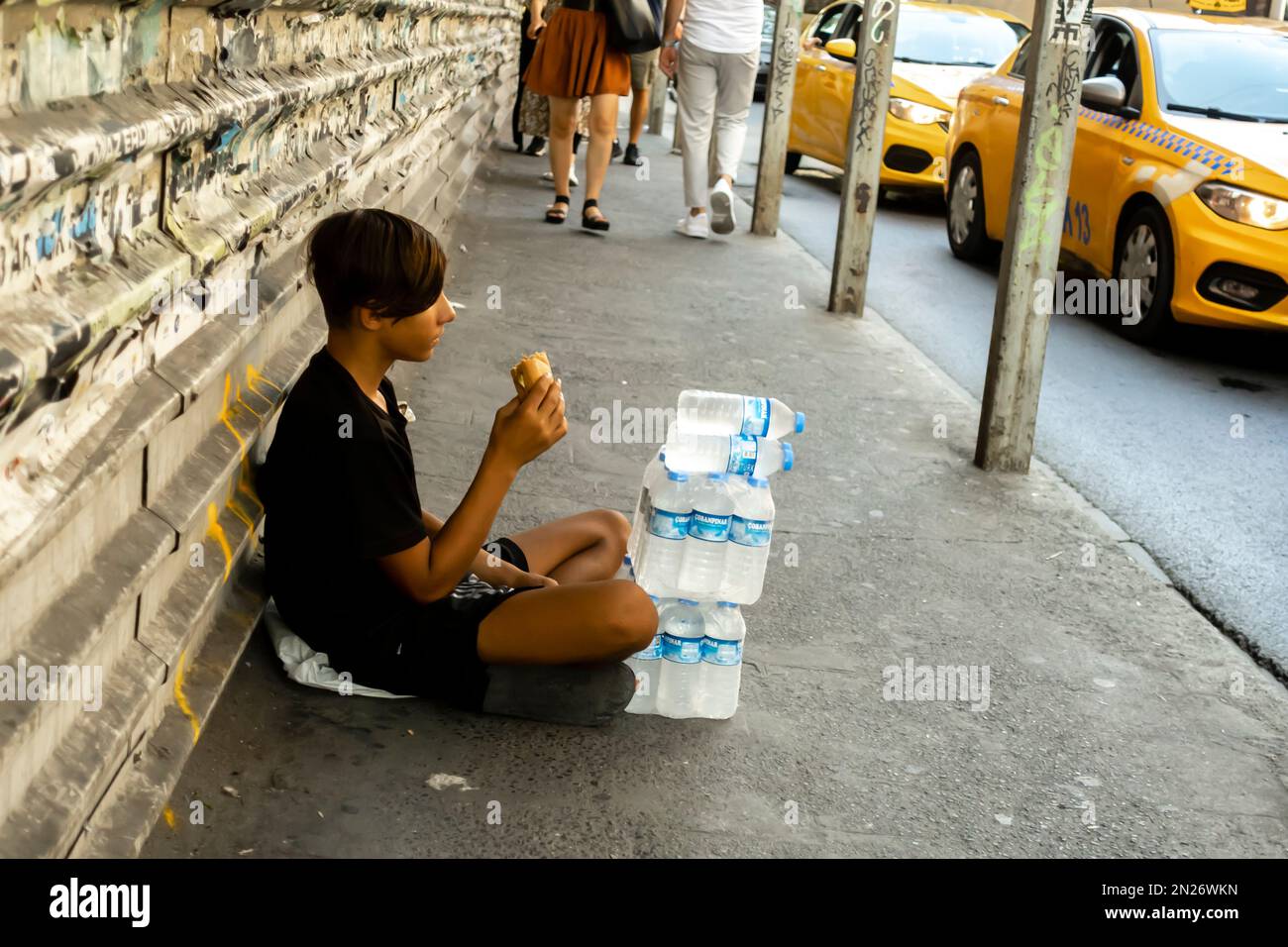 A boy selling bottles of water in a walking area near the road ...