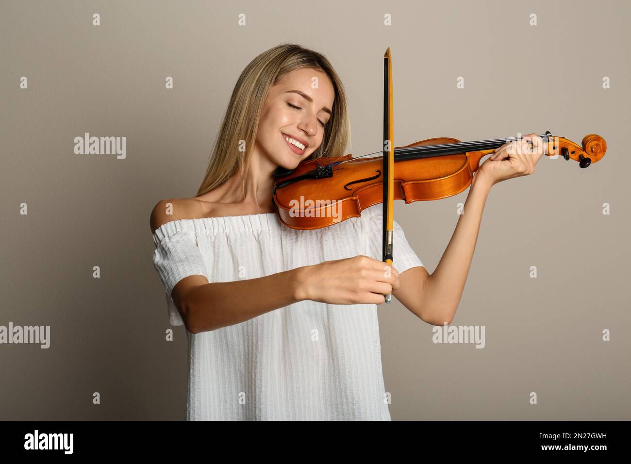 Beautiful woman playing violin on beige background Stock Photo - Alamy