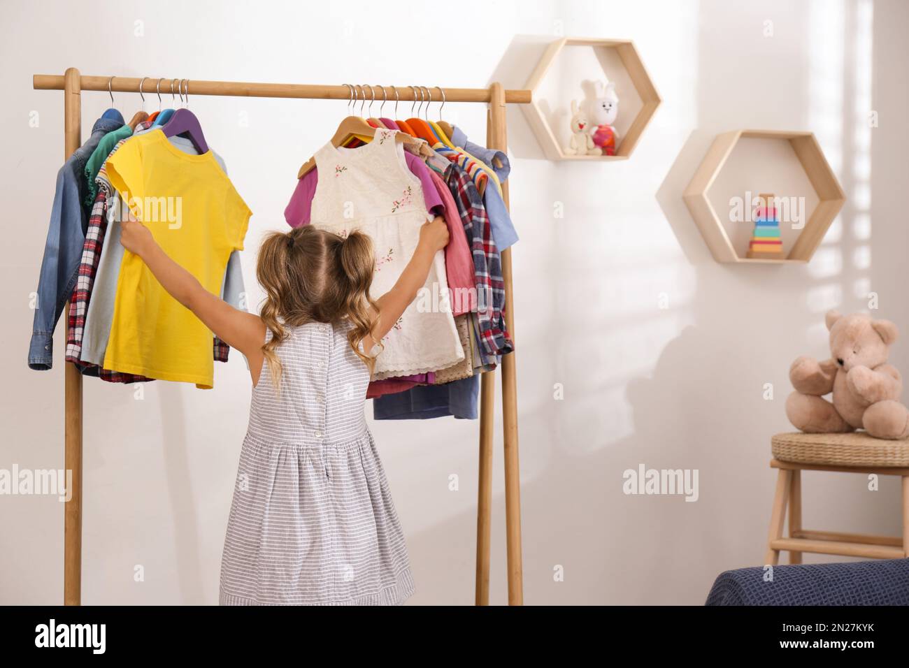 Little girl choosing clothes on rack in room Stock Photo - Alamy