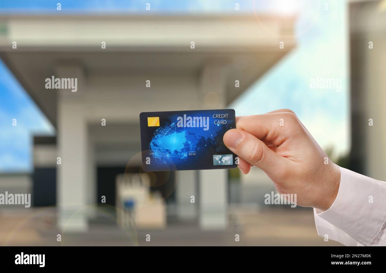 Man holding credit card against blurred gas station, closeup. Cashless ...