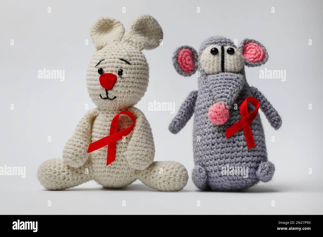 Cute knitted toys with red ribbons on light grey background. AIDS ...