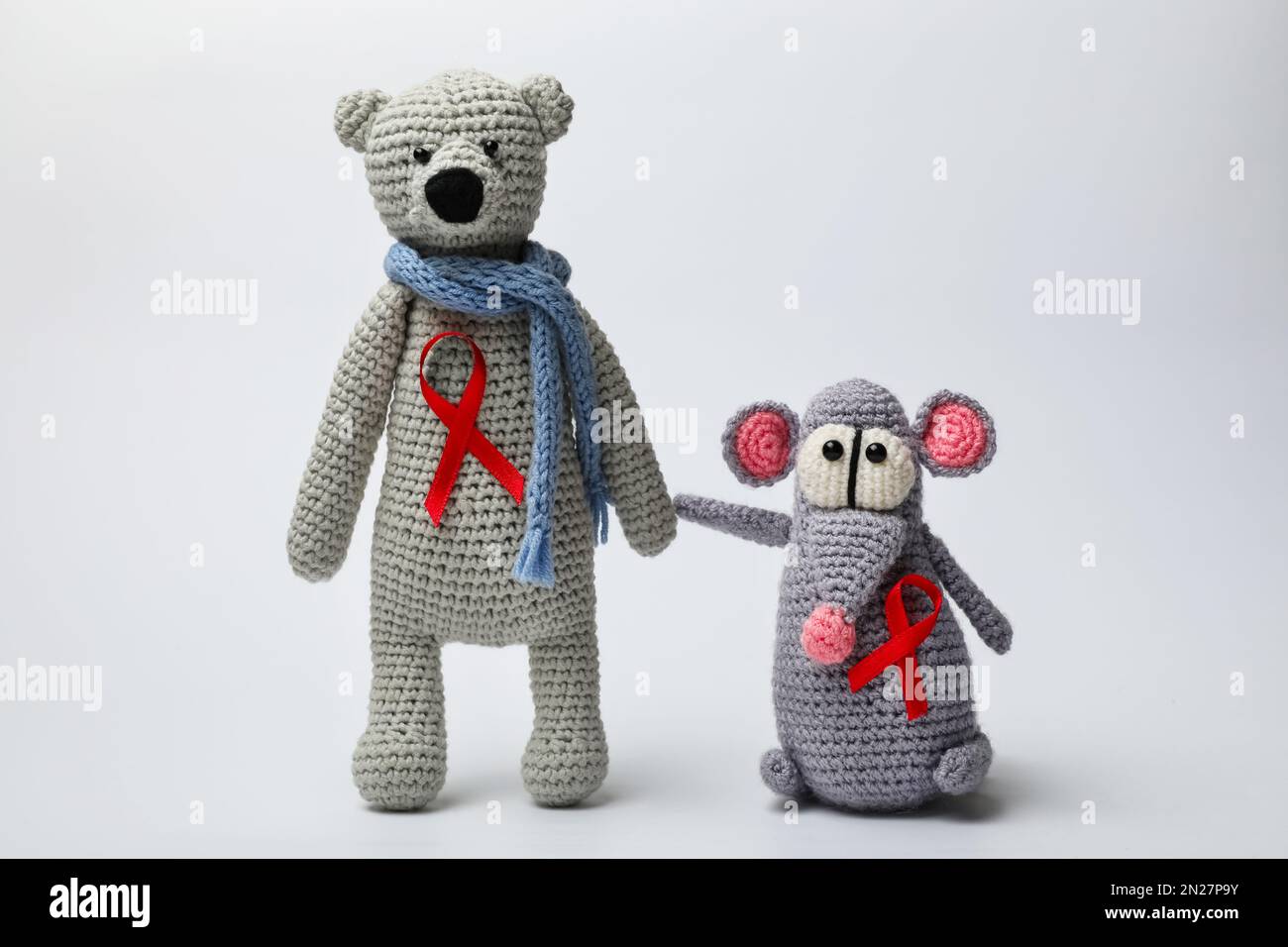 Cute knitted toys with red ribbons on light grey background. AIDS ...