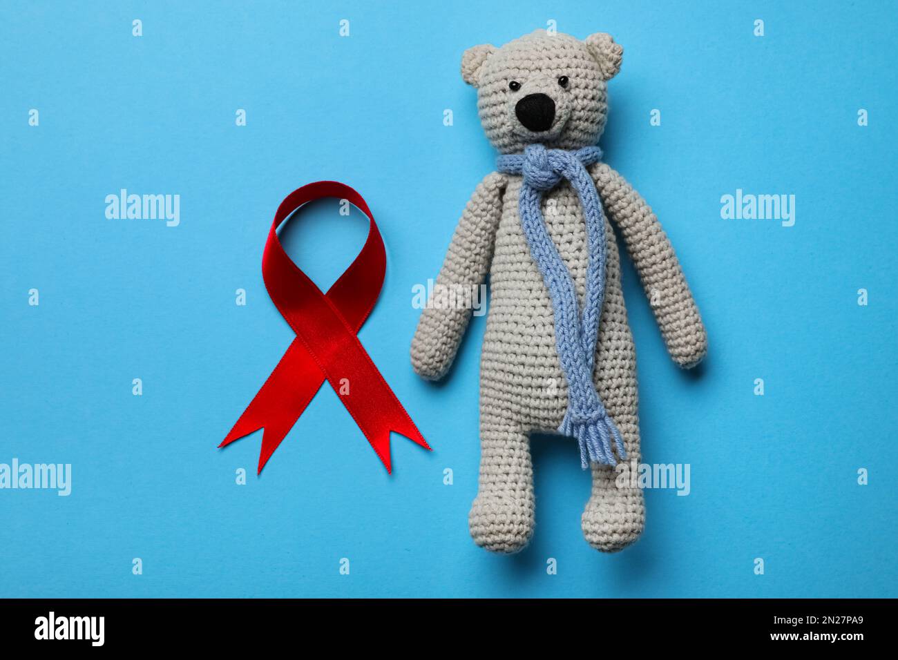 Cute knitted toy bear and red ribbon on blue background, flat lay. AIDS ...