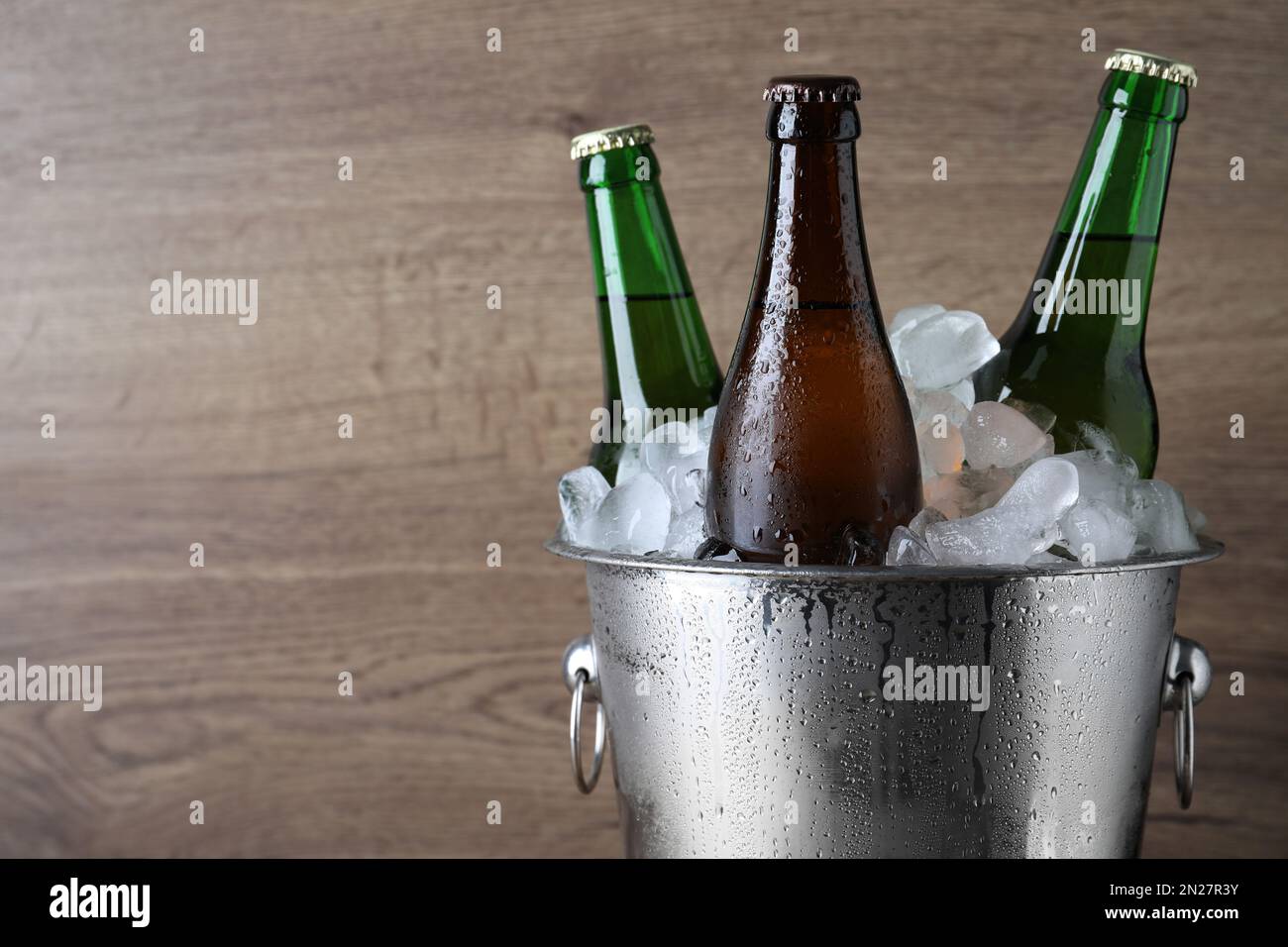 Metal bucket with bottles of beer and ice cubes on wooden background ...