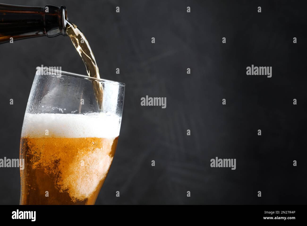 Pouring cold tasty beer from bottle into glass on black background ...