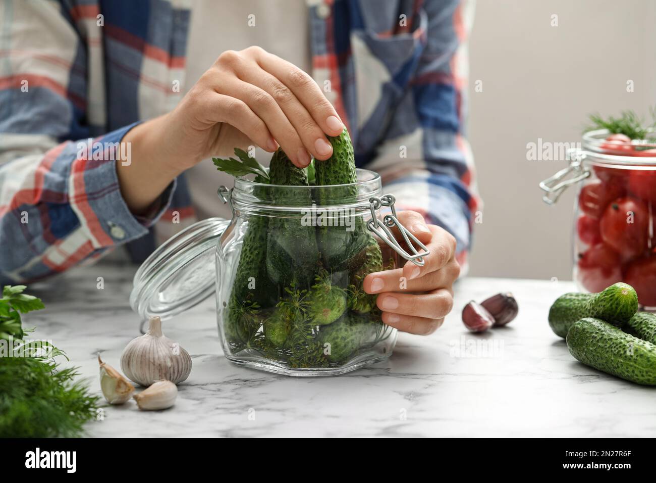 Woman putting cucumber into glass jar at white marble kitchen table ...