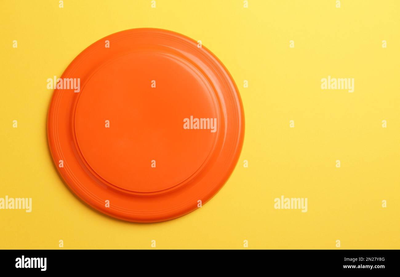 Orange plastic frisbee disk on yellow background, top view. Space for ...