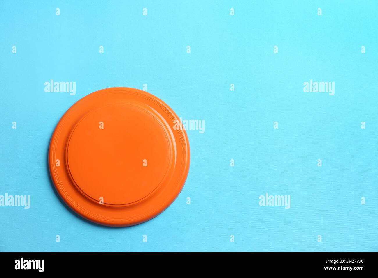Orange plastic frisbee disk on light blue background, top view. Space ...