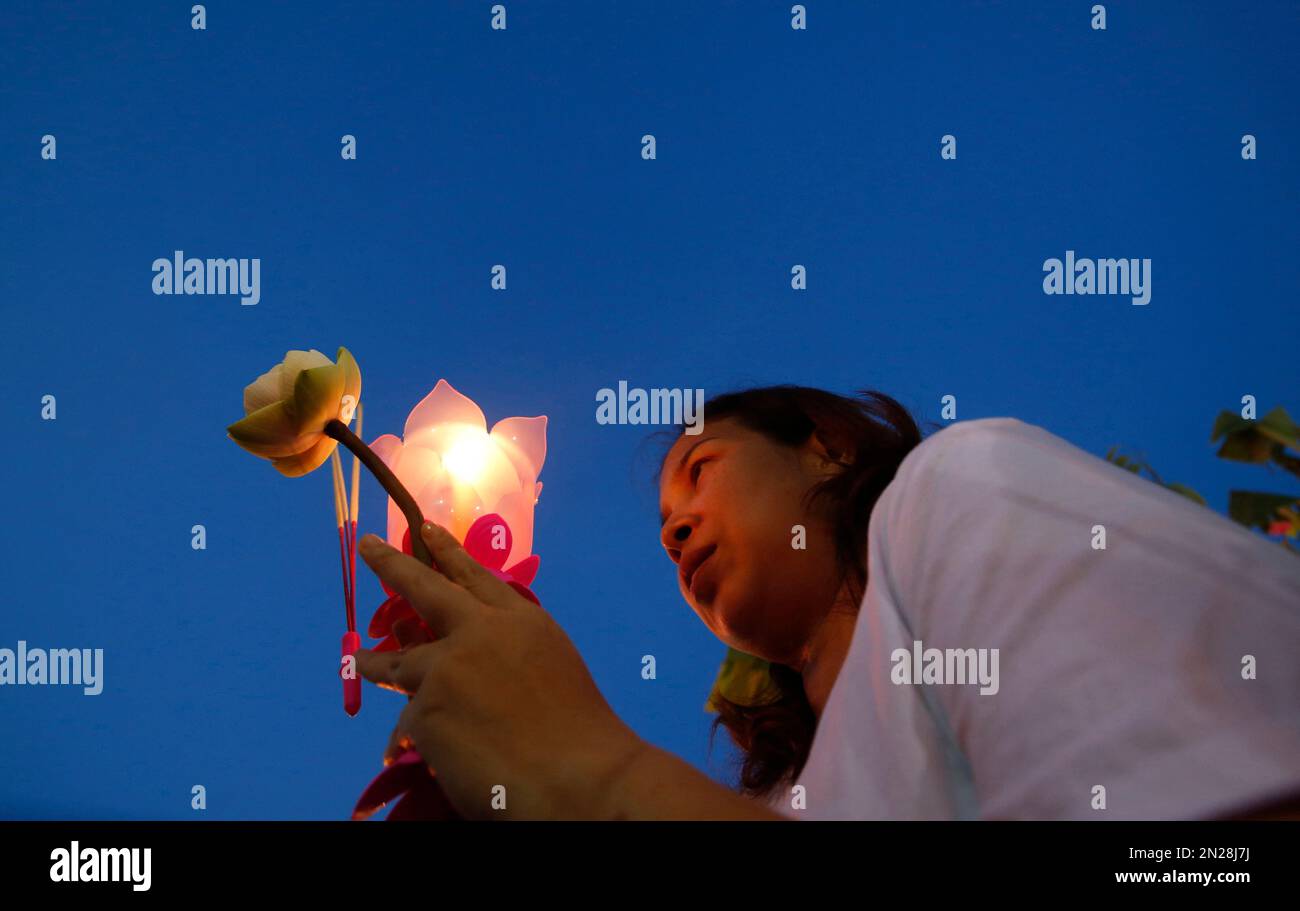 A Thai Buddhist carrying a candle and a lotus bud prays in front of ...