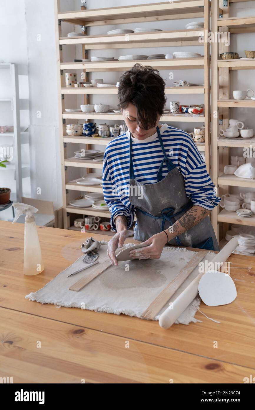 Creative focused womanpottery artist stands at table in own workshop ...