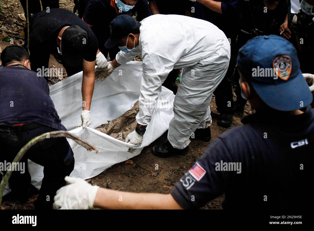 Malaysian police forensic team members excavate an unmarked grave in ...